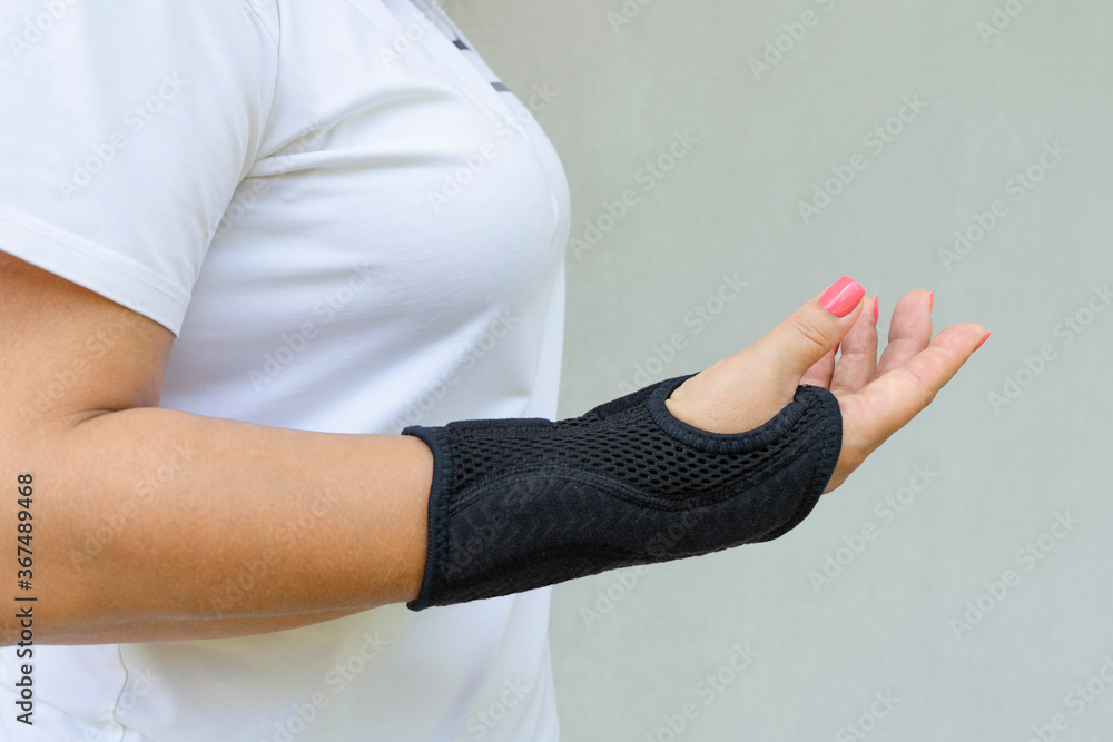 Black wrist brace or corset is worn on women's hand for treatment of ...