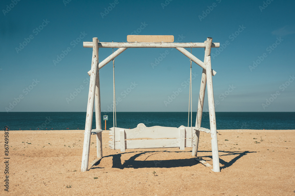 Swing on the seashore. Swing-bench on a sandy beach next to the sea ...