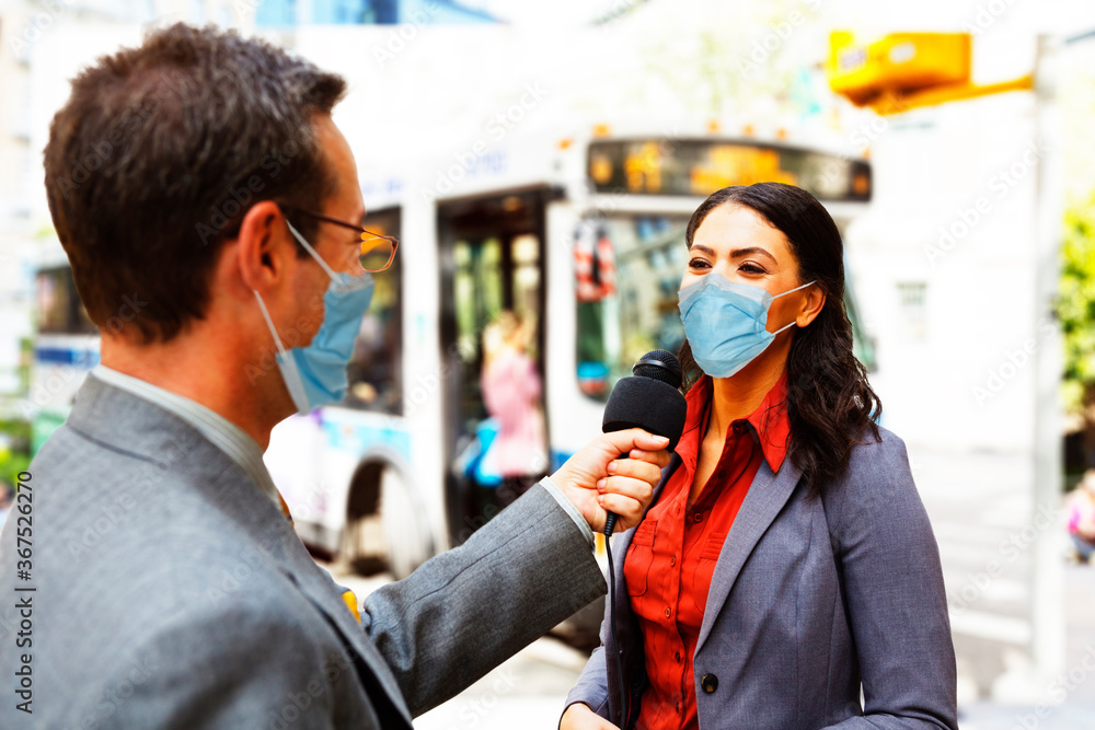 A reporter with a microphone interviews a woman on a city street. Both ...