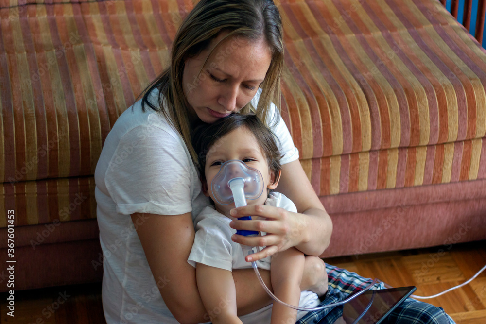 Young mother hold mask vapor inhaler to little boy breathing through ...
