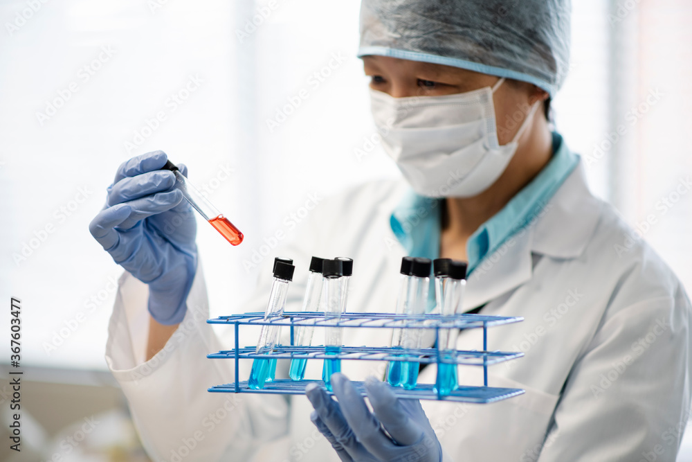 Medical researcher in PPE looking at test tube samples in laboratory ...