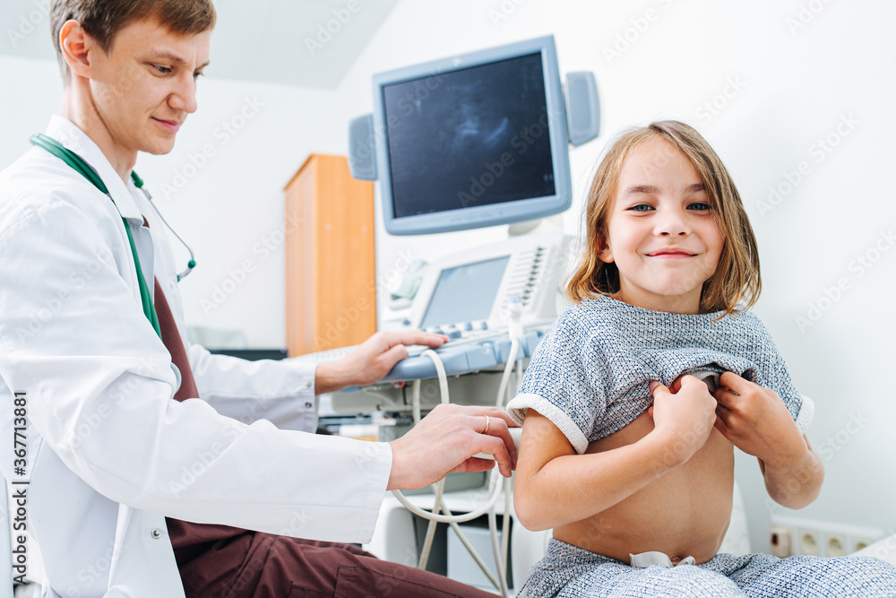Little girl smiling at camera while being scanned with ultrasound probe ...