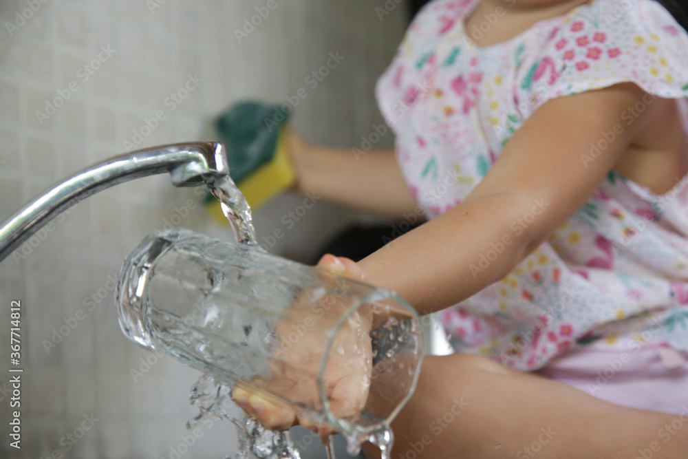 Child washing dishes in the kitchen. Cute two year old girl washes ...