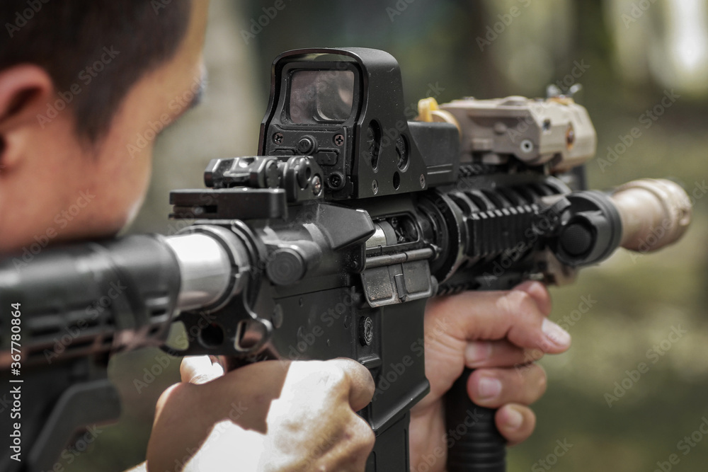 Military shooter with his precising assault rifle aiming and shooting ...