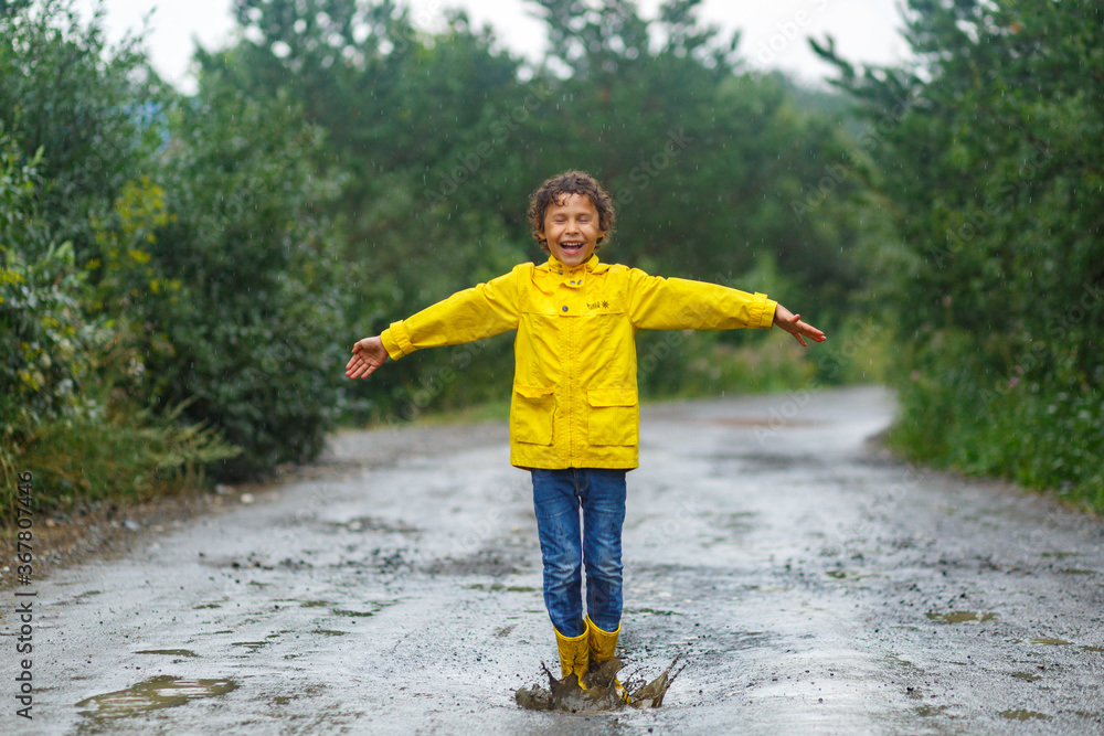 Kid playing in the rain in autumn park. Child jumping in muddy puddle ...