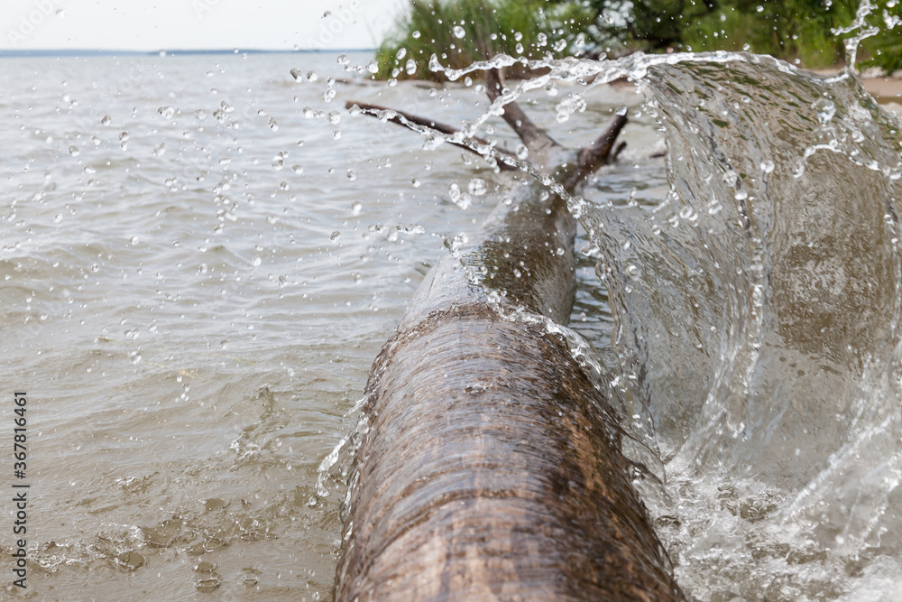 The beating waves of the river against a log near the sandy shore wash ...