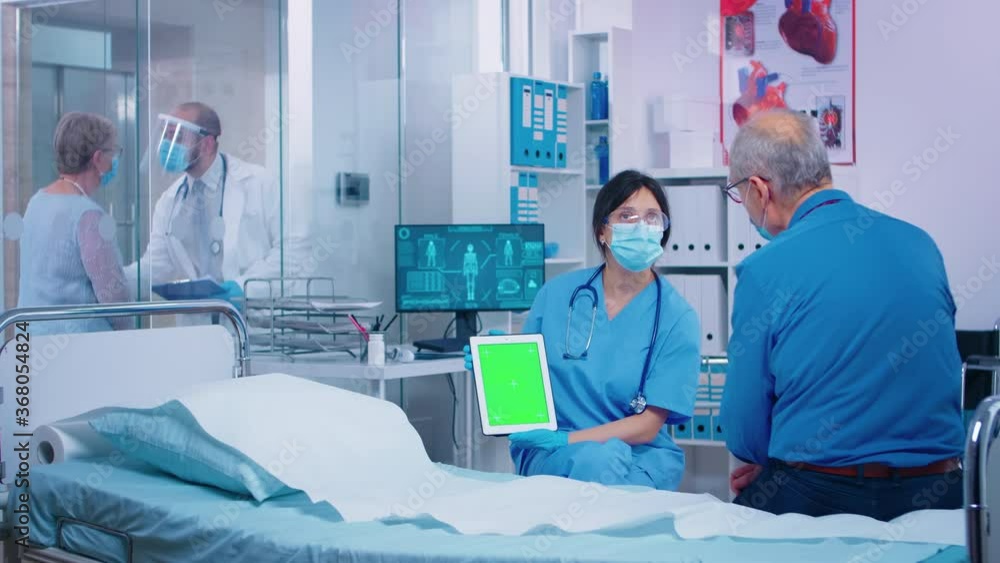 Nurse presenting green screen tablet to patient in modern private ...