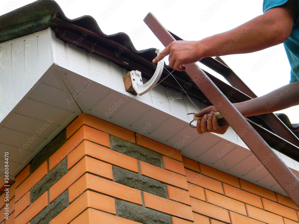 A building contractor is installing rain gutter system, fitting ...