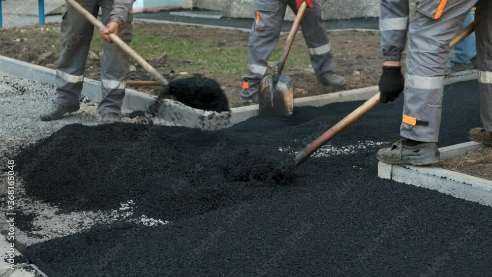Workers pour asphalt with a shovel . Loosening and leveling of heated ...