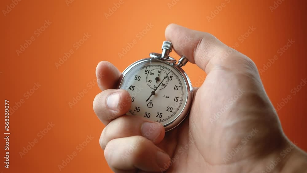 Male hand holding analogue stopwatch on orange color background. Time ...