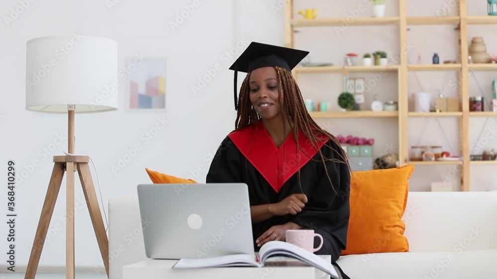woman in graduation costume gestures and smiles when video calling ...
