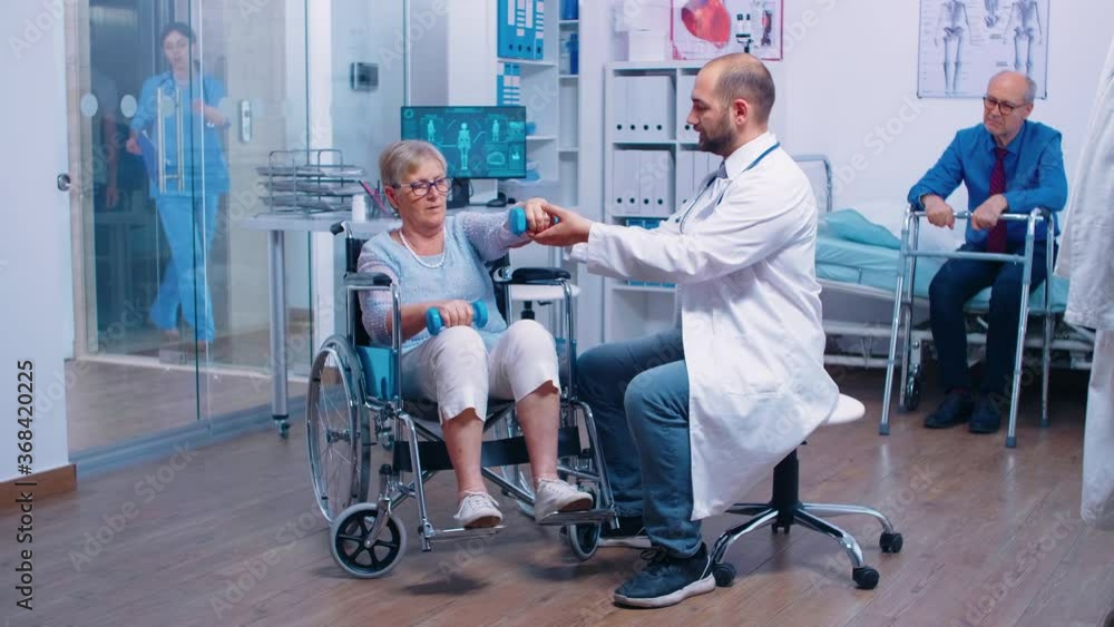 Doctor helping old disabled woman in wheelchair to regain muscle ...