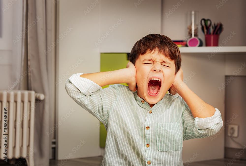 Little autistic boy with strong negative face expression closing ears ...