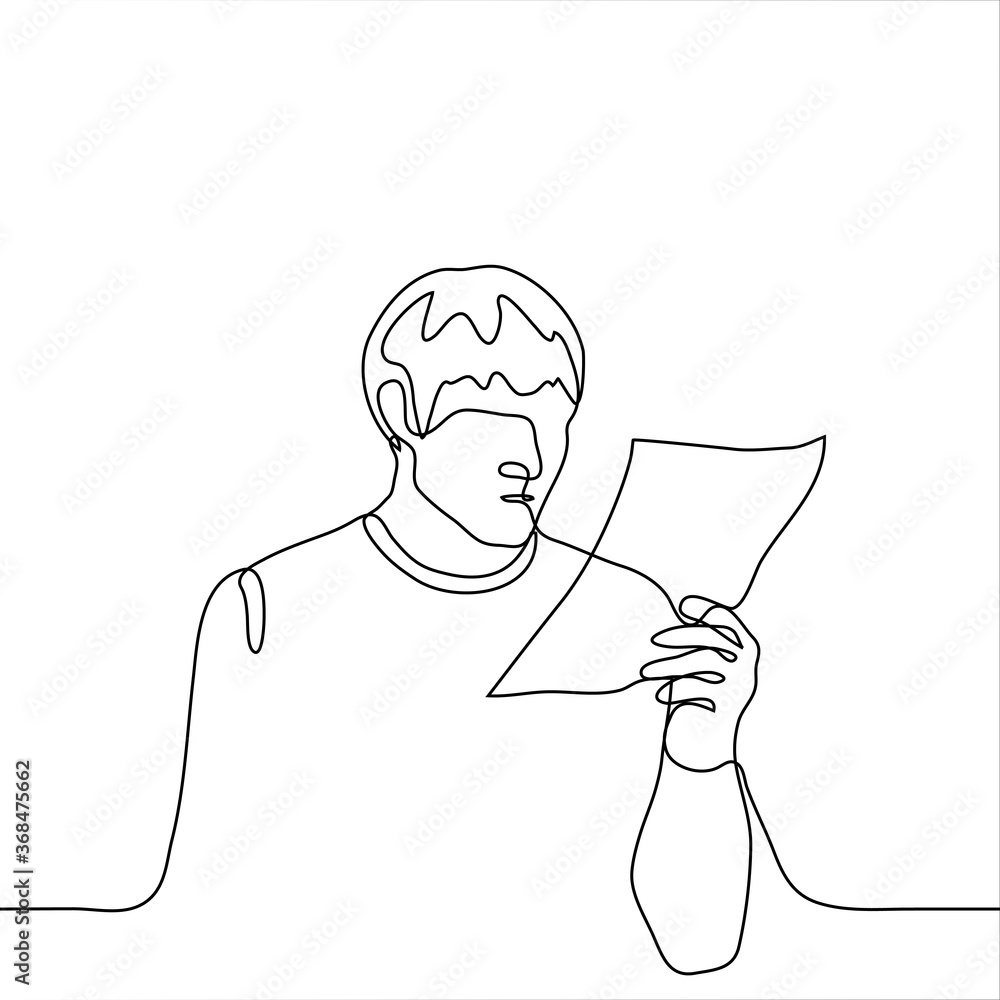 young man holds a sheet of paper in front of his face and reads it ...