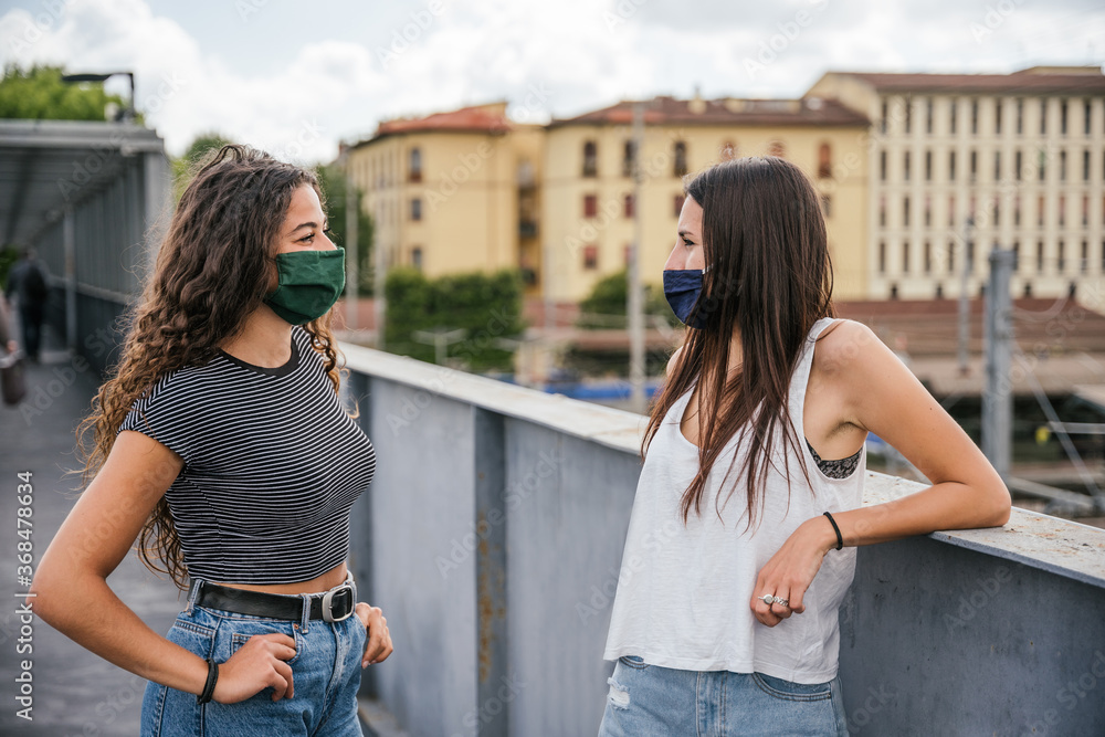 Two young best friends meeting on iron bridge wearing a face mask to ...
