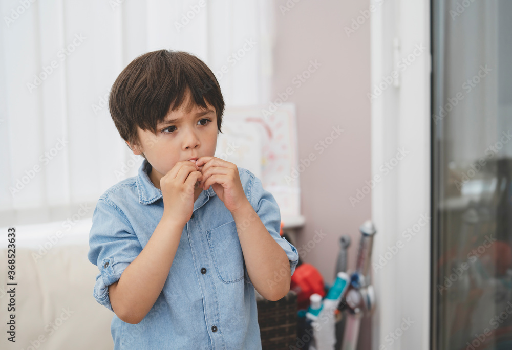 Portrait of kid biting his finger nails while looking at something ...
