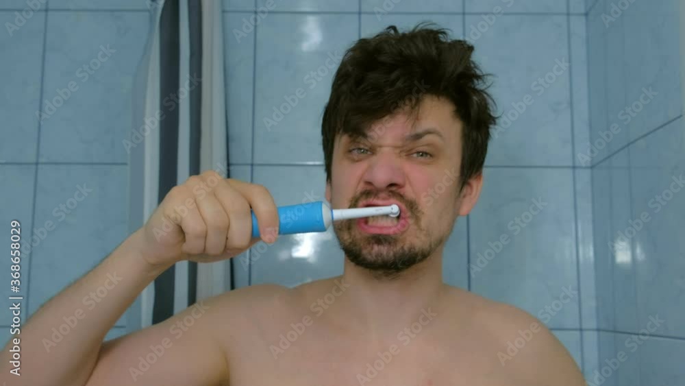 Funny man is brushing teeth usin electric toothbrush and making ...