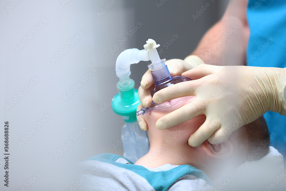 An anesthesiologist holds a breathing mask over the face of a young boy ...