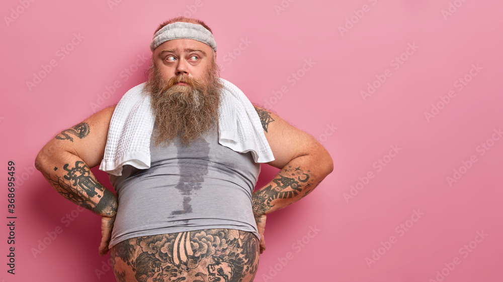 Pensive stout man has deep thoughts, keeps hands on waist, works hard ...