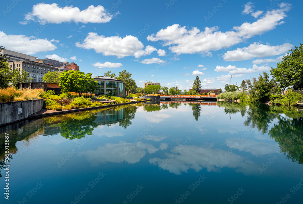 The summer blue sky with clouds reflects off of the Spokane River at ...