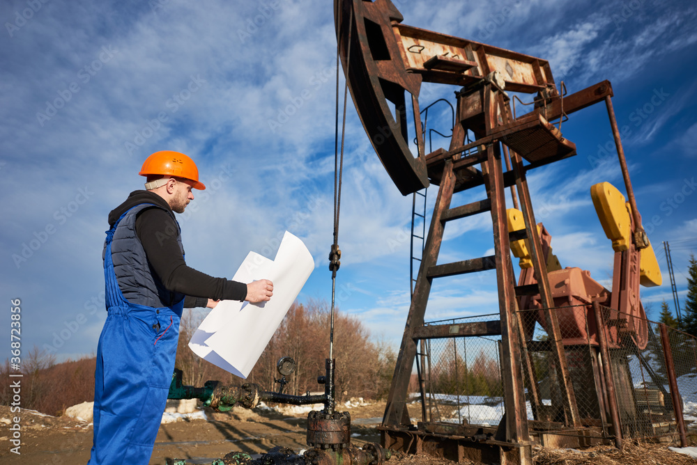 Side view of oil worker holding plan of oil field. Engineer in work ...