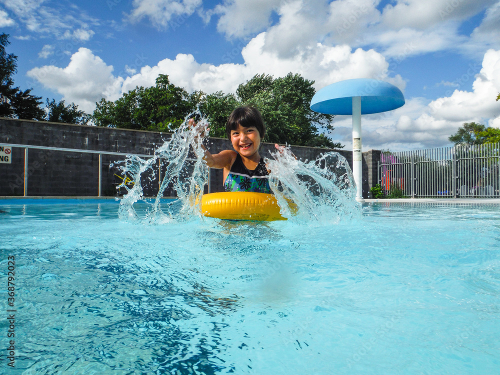 Cute little girl with floaty splashing water in an outdoor swimming ...