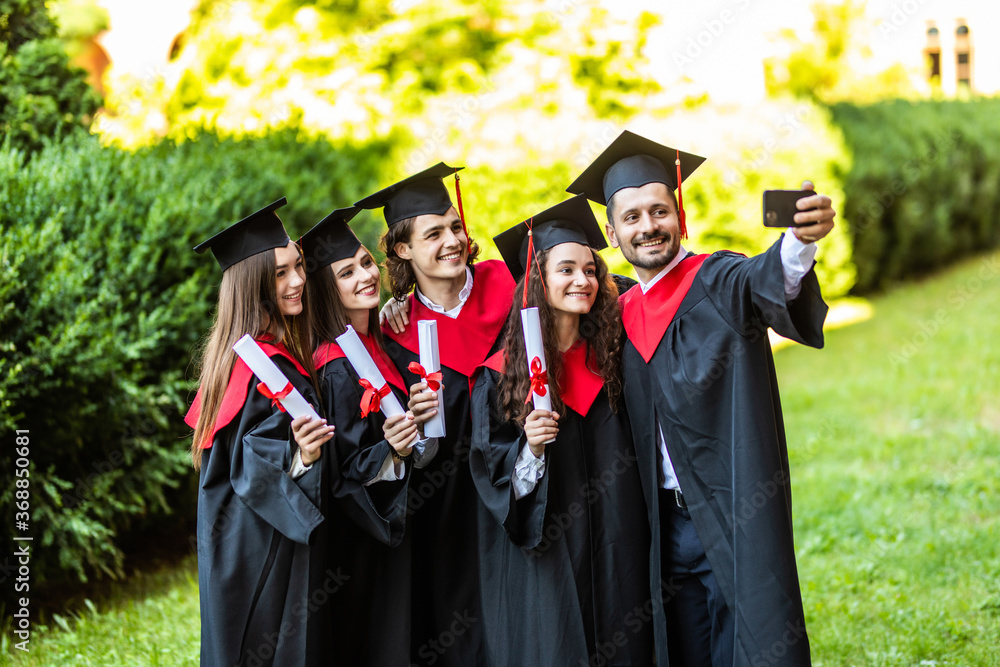 Capturing a happy moment. Four college graduates in graduation gowns ...