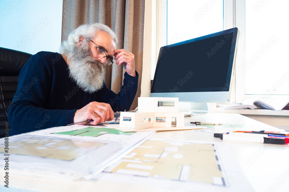 A man with gray hair and a beard looks thoughtfully at the model of the ...