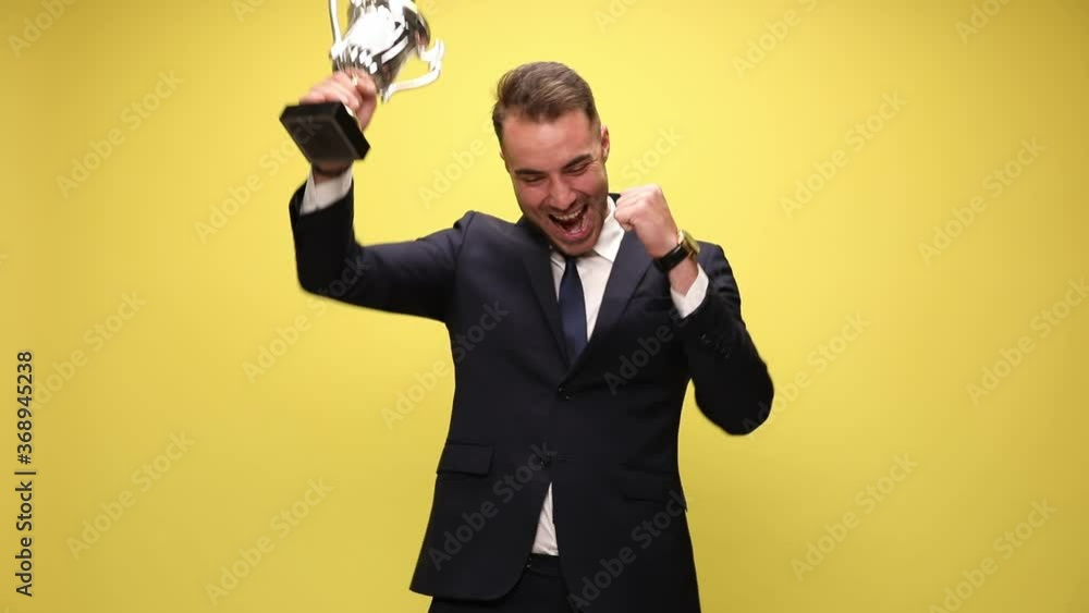 excited young businessman holding trophy, holding arms in the air and ...