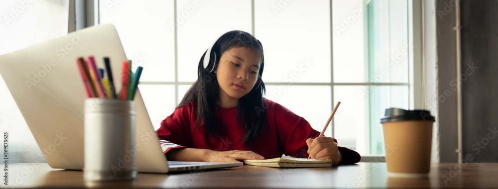 Female student wears headphones sitting at table to learning and note ...