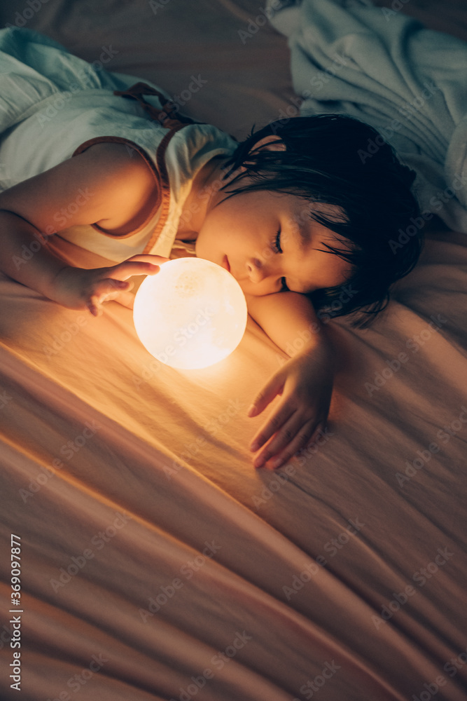 Little girl lying in bed holding a lamp Stock Photo | Adobe Stock