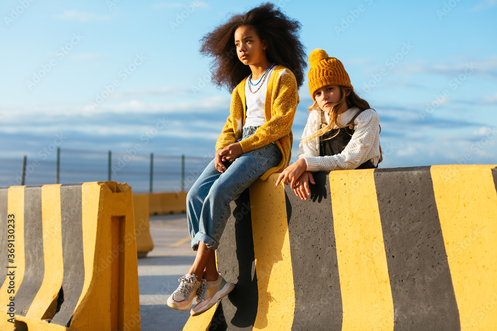 Fashionable multiethnic children sitting on street barrier fence Stock ...