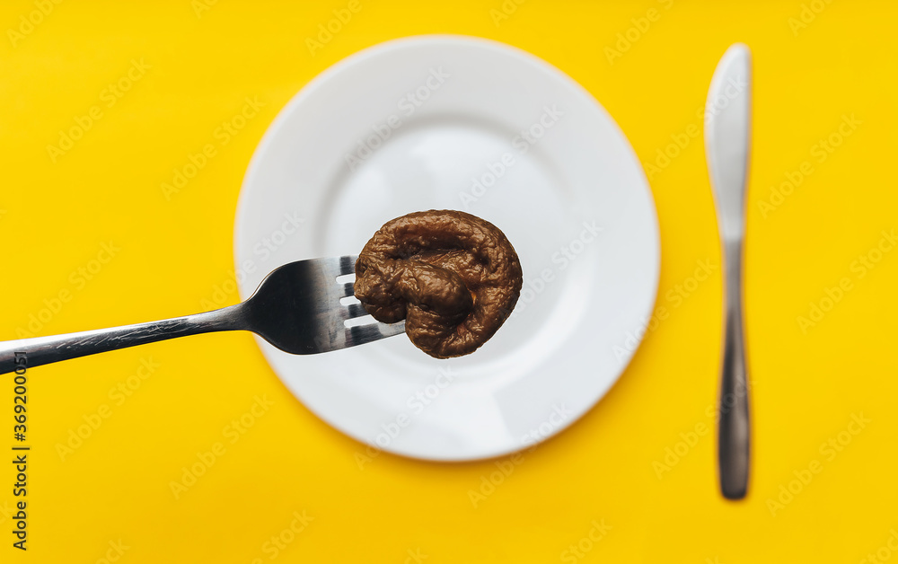 Artificial cat feces lie on a fork close-up. White plate and a knife ...