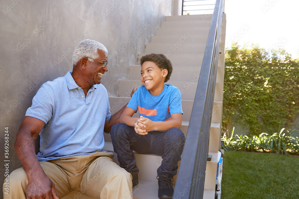 Grandfather With Grandson Sitting On Steps And Talking Outdoors At Home ...