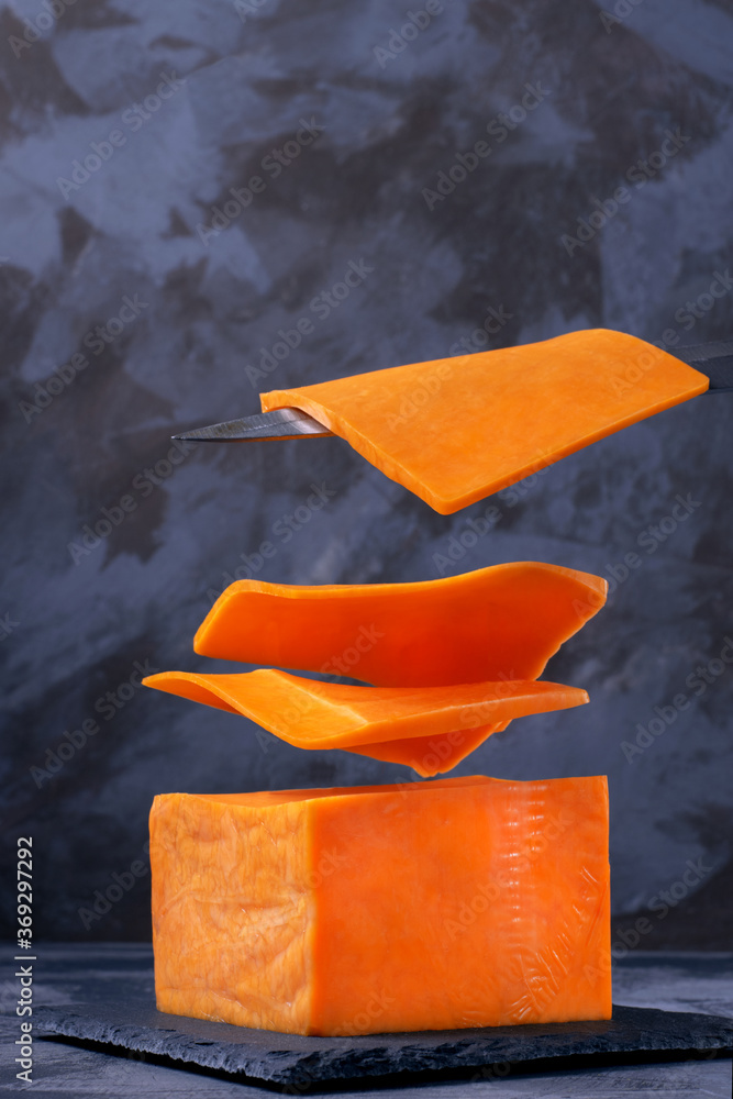 Levitating slices of red Cheddar cheese against the grey background ...