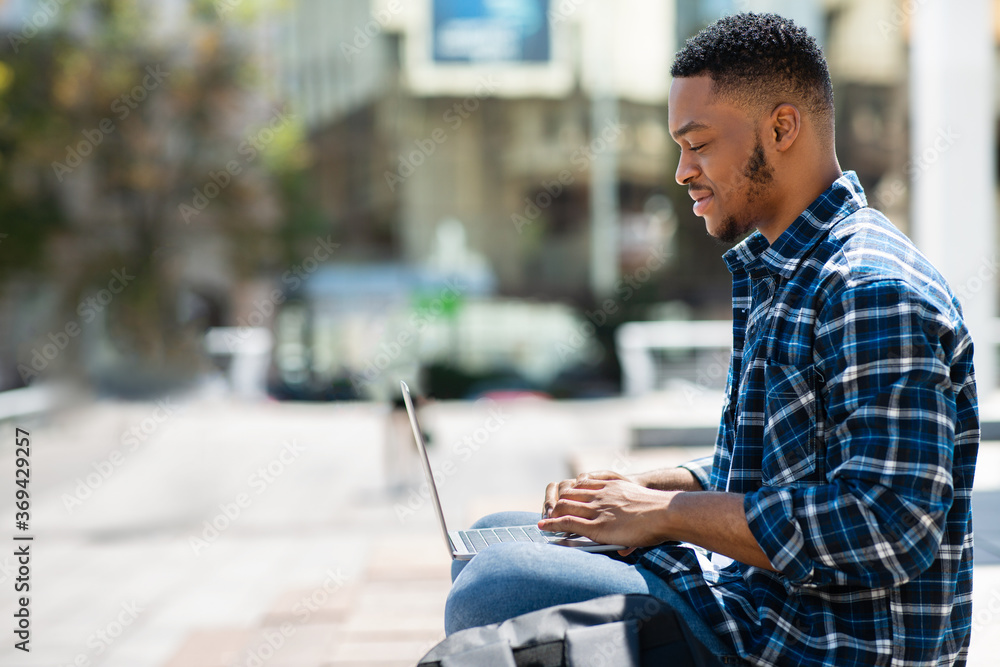 Black man using laptop, sitting in downtown with gadget Stock Photo ...