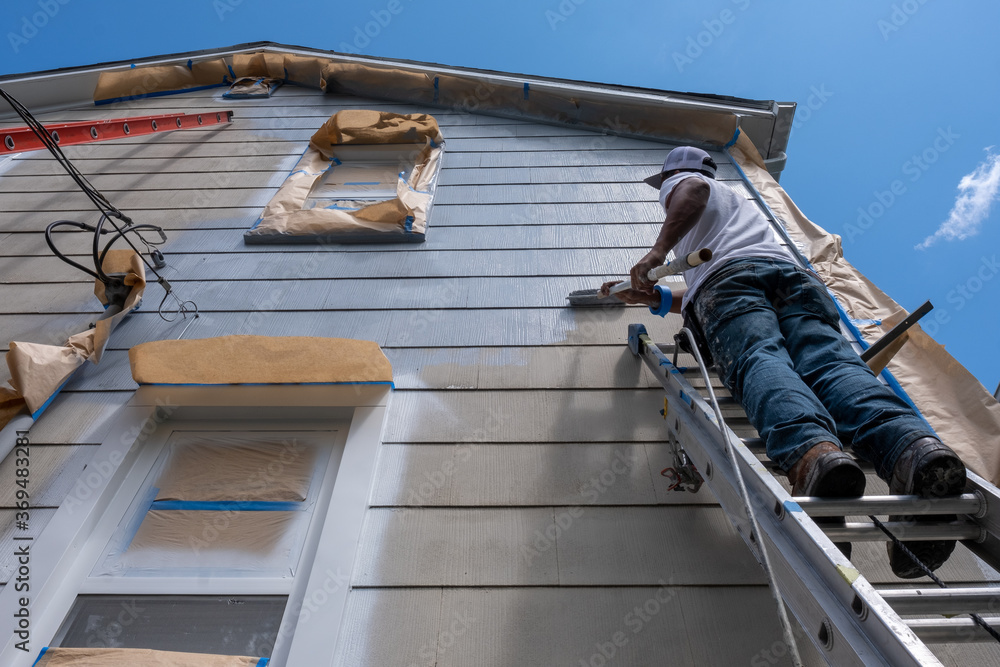 Painter on a ladder rolling paint onto the exterior of a house Stock ...