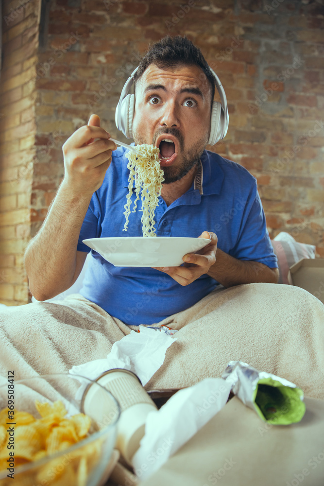 Foto de Shocked eating instant noodle, watching TV. Lazy man living in ...