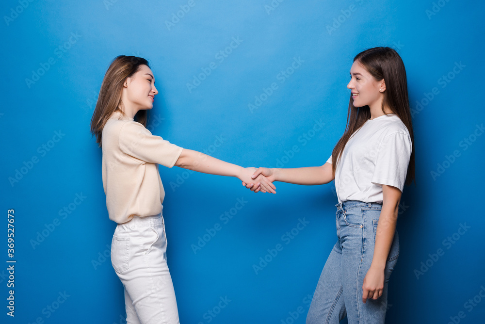 Two young women, standing and dressed casually, shaking hands and ...
