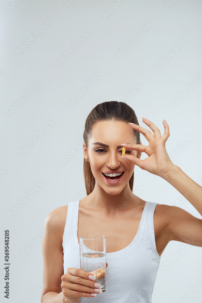Portrait of beautiful woman taking vitamin pill with glass of fresh ...