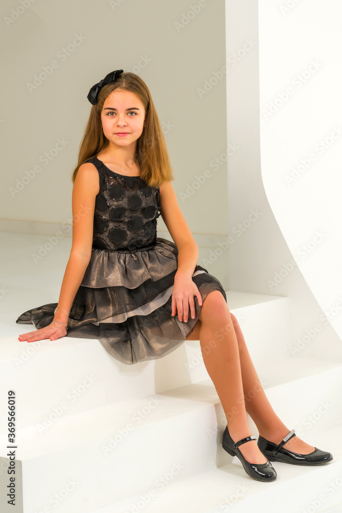 Cute little girl is sitting in the studio on the white stairs. style ...