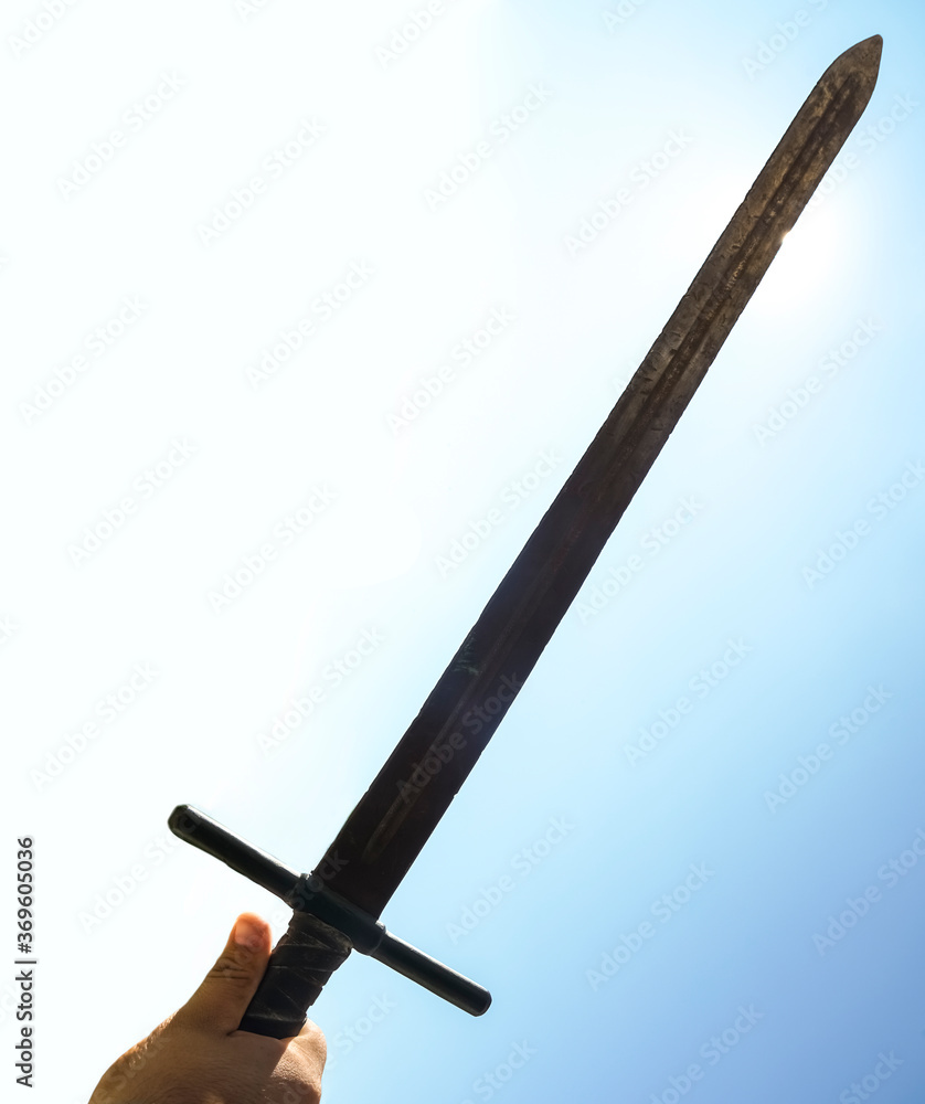 historical sword in male hand on blue sunny sky background. no face ...