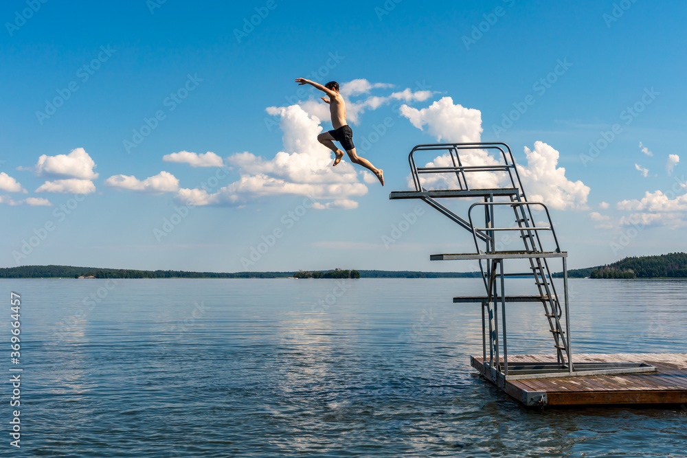 Side view of a teenage male jump diving from a diving tower with blue ...