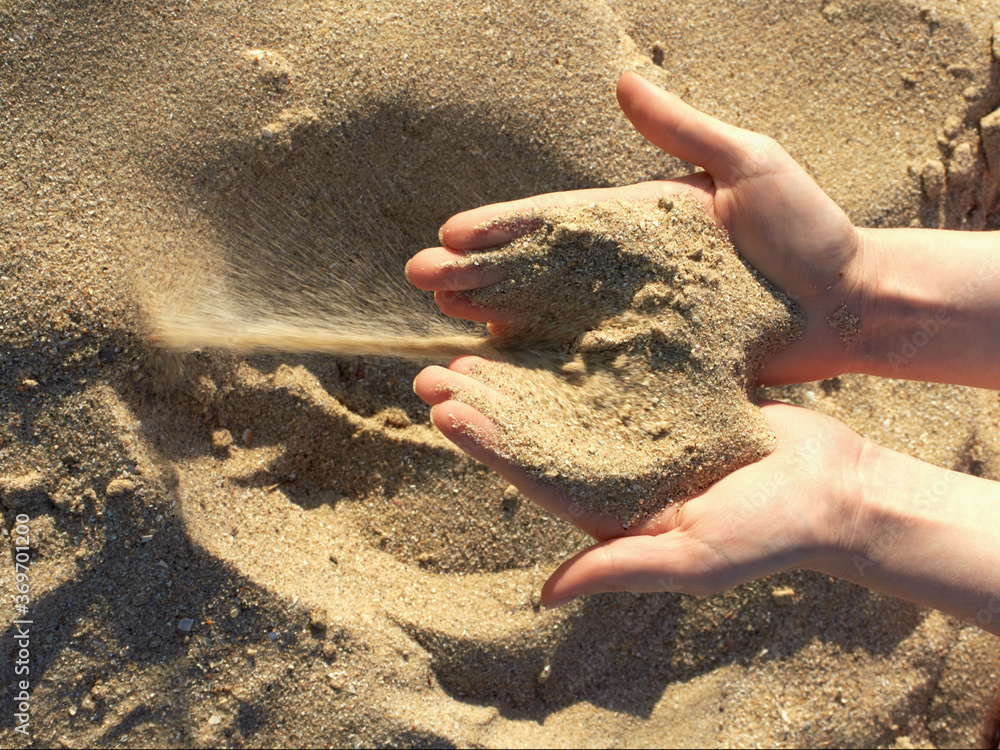 top view of the hands through which the sea sand is pouring. time flies ...