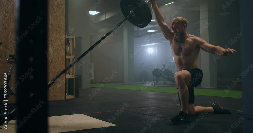 A male athlete lifts a weight bar with one hand in slow motion ...