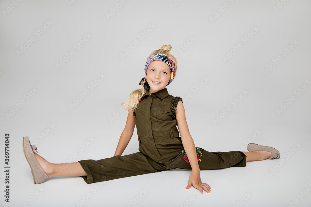 Girl child sits easily at ease in splits on light background and smiles ...