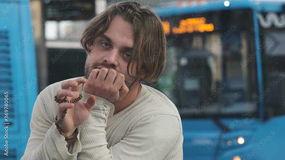 homeless looking hipster sits at bus stop behind the glass in city and ...