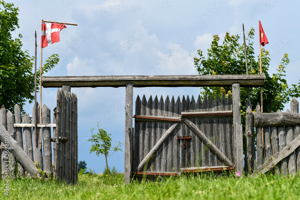 Wooden gate and fence to the ancient fortress with a red flag waving ...