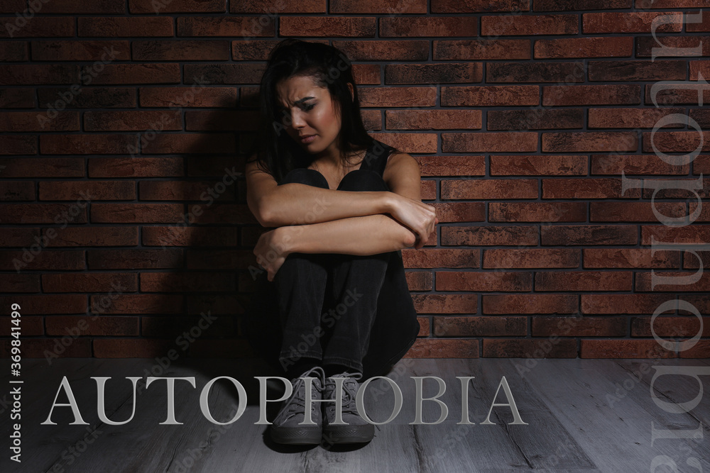 Depressed young woman sitting alone near brick wall. Autophobia - fear ...