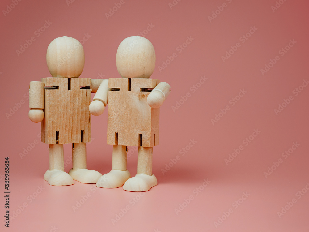 2 wooden dolls hugging each other on a pink background. Concept of ...